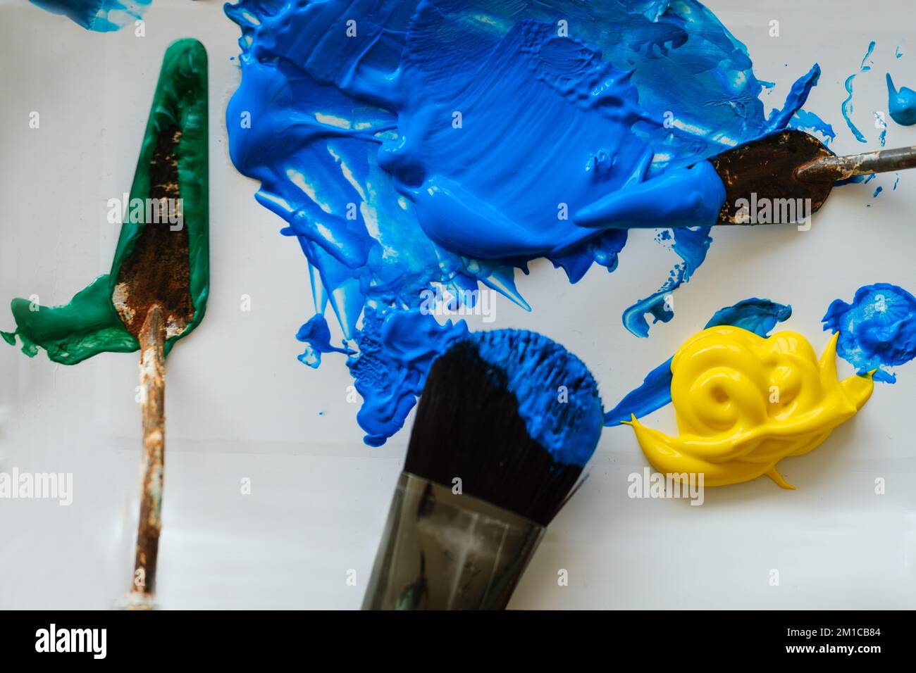 Overhead shot of brushes for painting, puddle of blue, and yellow paint ...