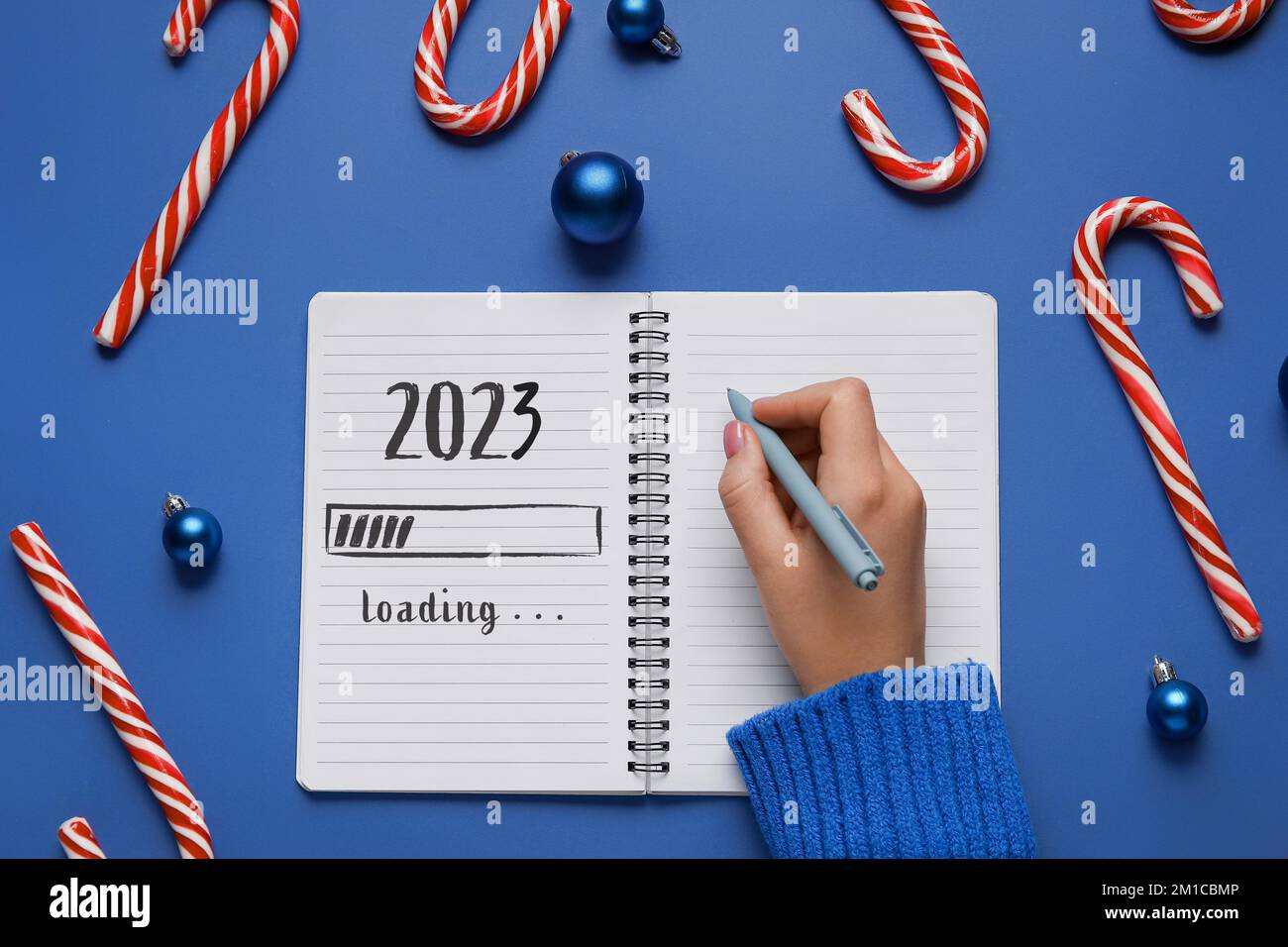 Woman making to-do list for year 2023 on blue background, top view ...