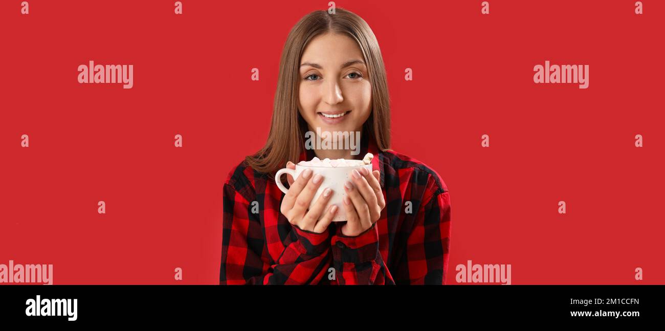 Pretty young woman in pajamas drinking hot chocolate on red background ...