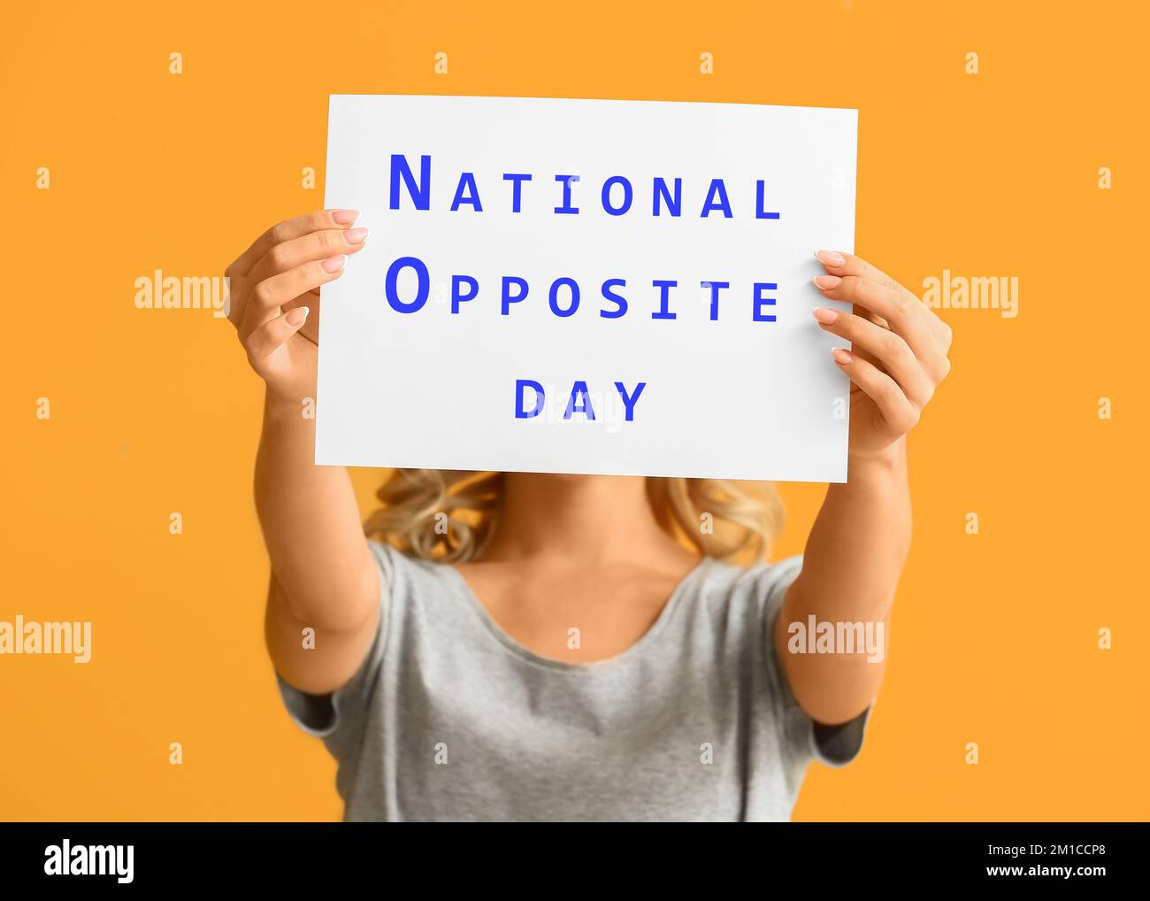 Woman holding paper sheet with text NATIONAL OPPOSITE DAY on orange ...