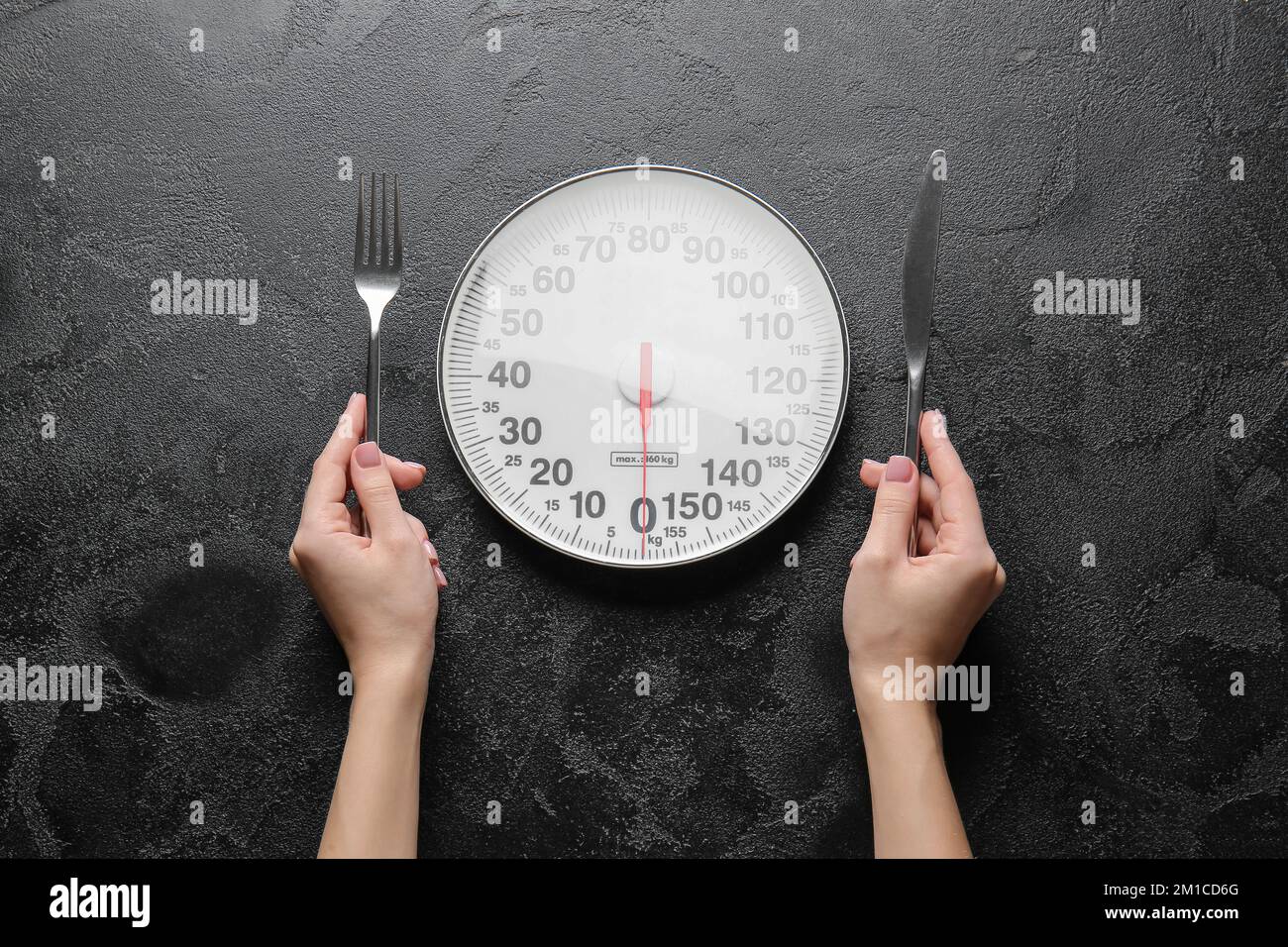 Female hands with weight scales and cutlery on dark background. Diet ...