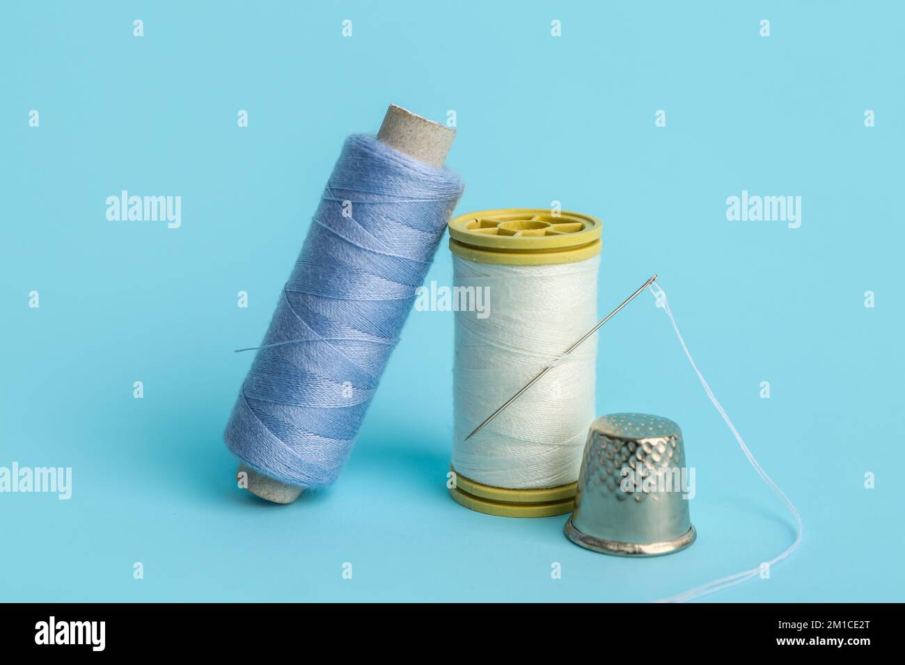 Thread spools with needle and thimble on color background Stock Photo ...
