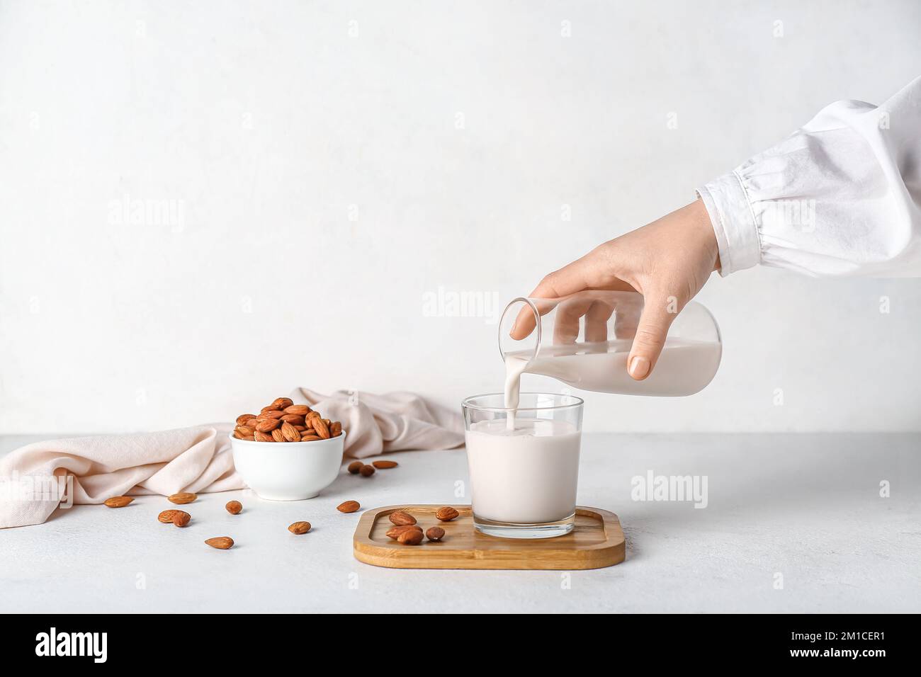 Woman pouring almond milk into glass on white table Stock Photo - Alamy