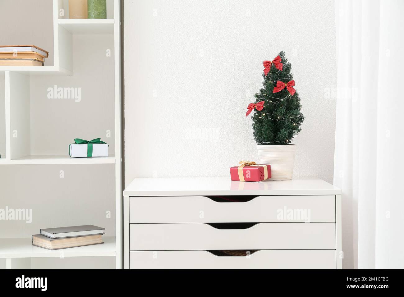Small Christmas tree with glowing lights and gift on chest of drawers ...