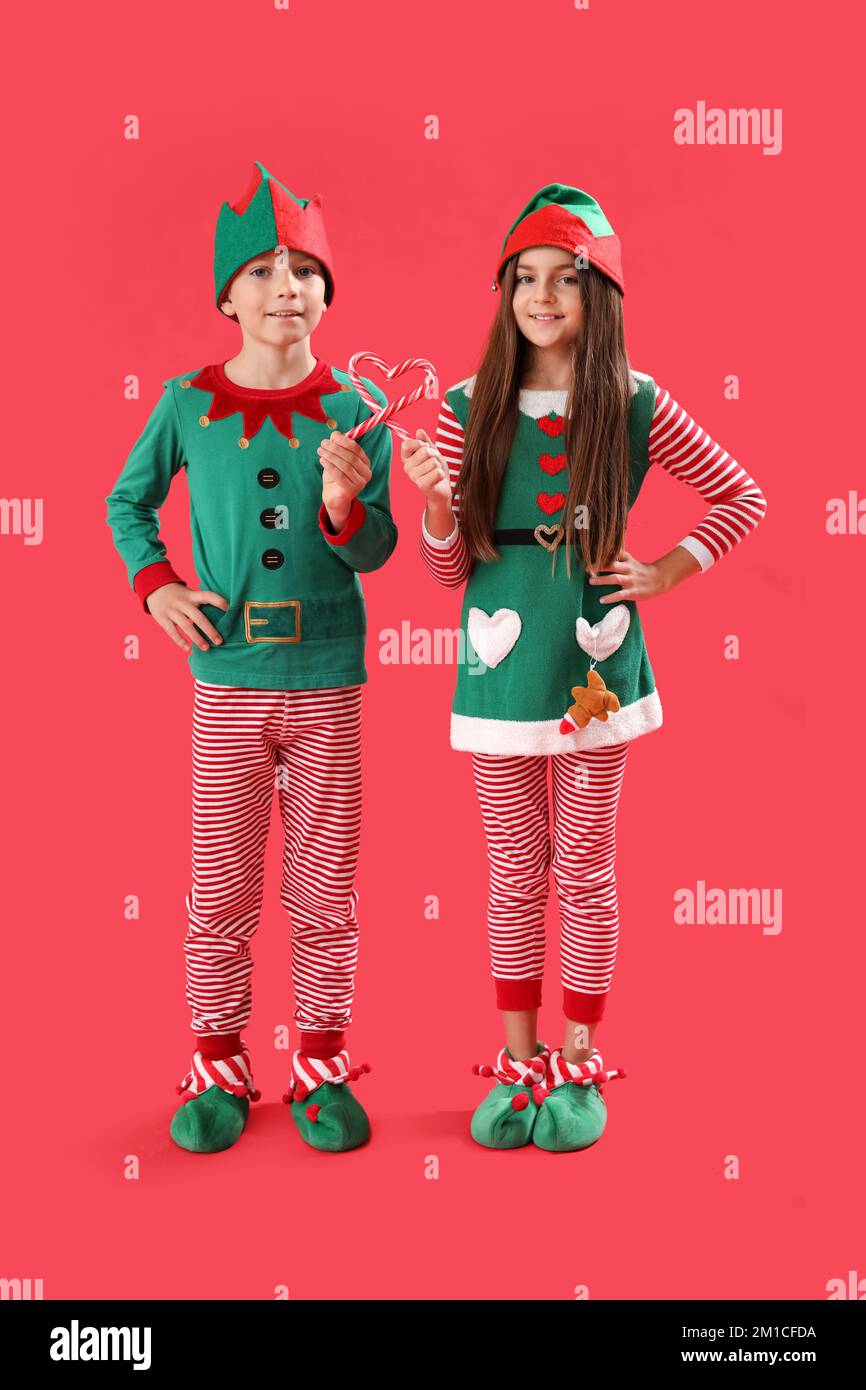 Little children in elf pajamas with candy canes on red background Stock ...