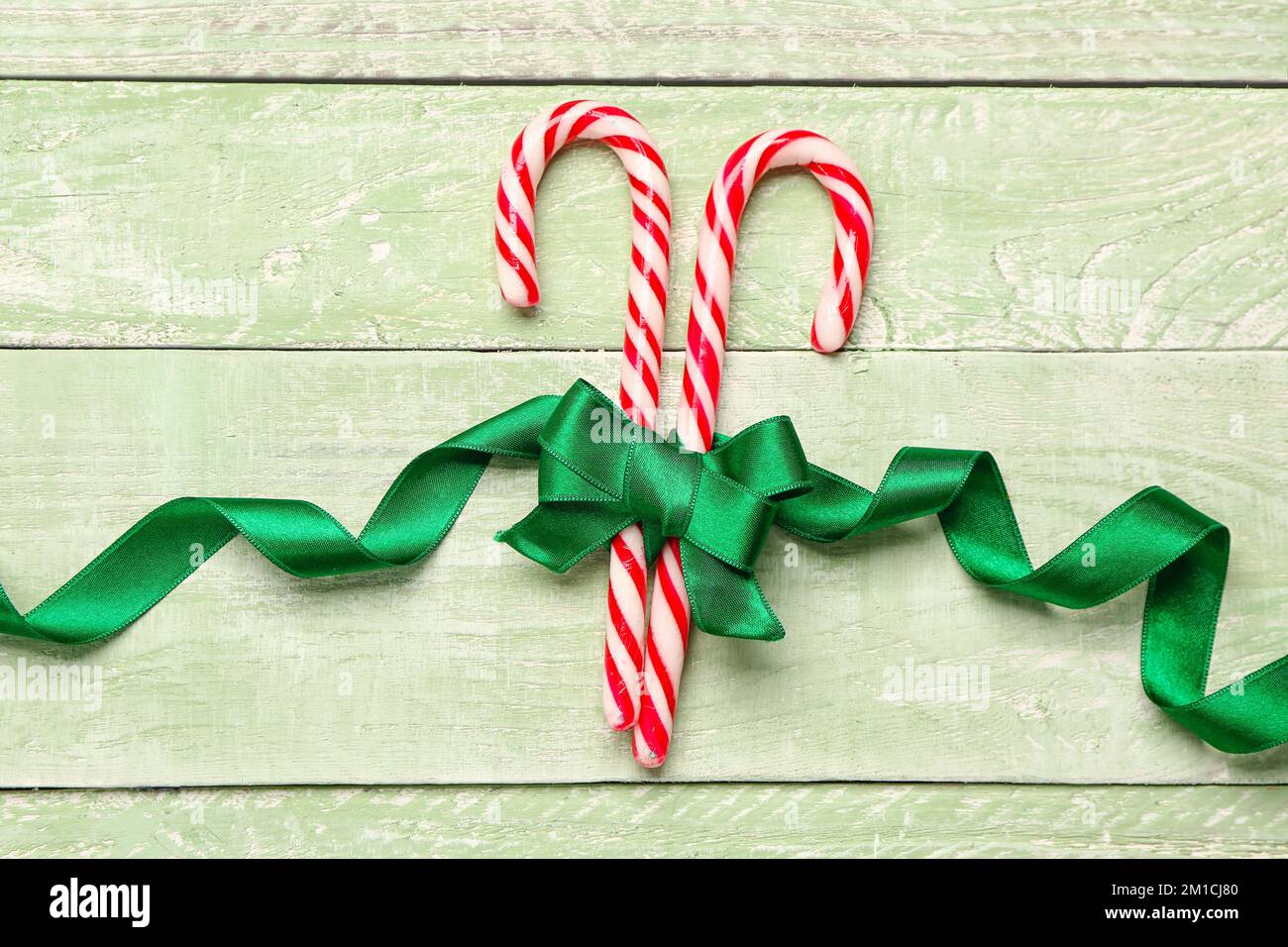 Sweet candy canes tied with green ribbon on color wooden background ...