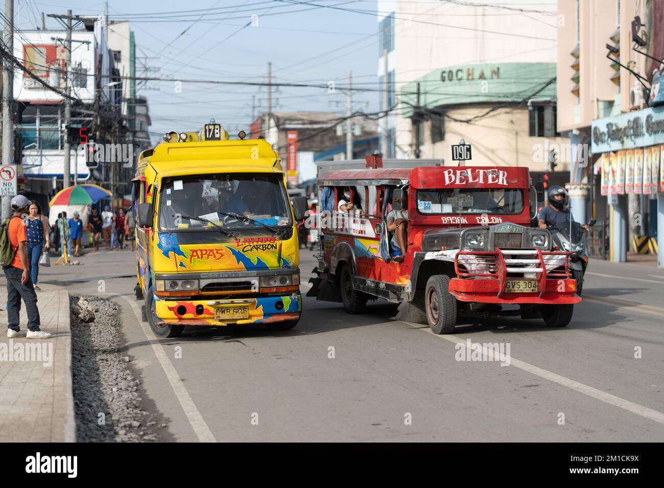 A yellow multicab alongside a red Jeepney. Both are use as public ...