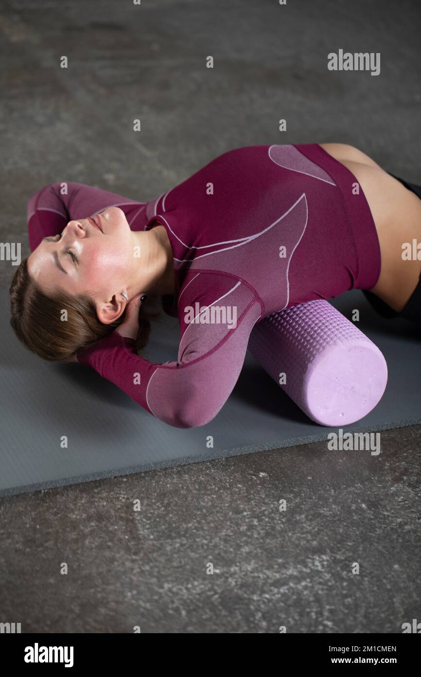 A woman performs a myofascial release for her back using a roll on a ...