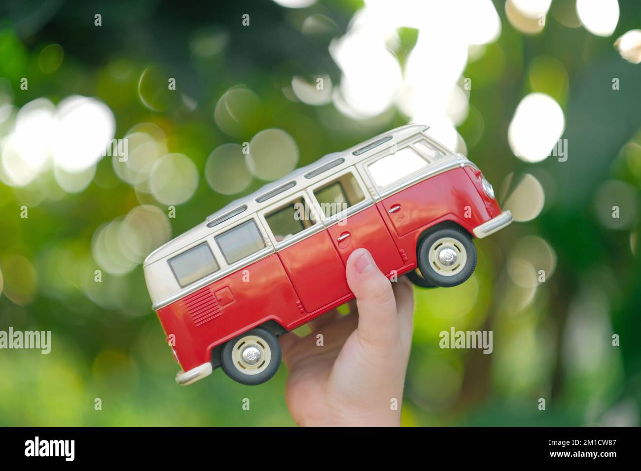 Young child's hand holds up a red toy car van against vibrant green ...