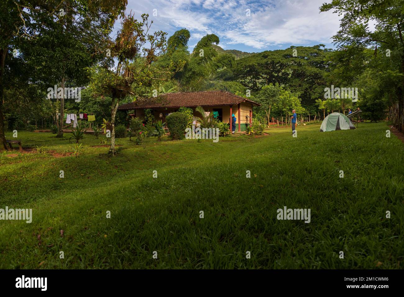A landscape of rural cabin and a camp tent on green meadows with trees ...