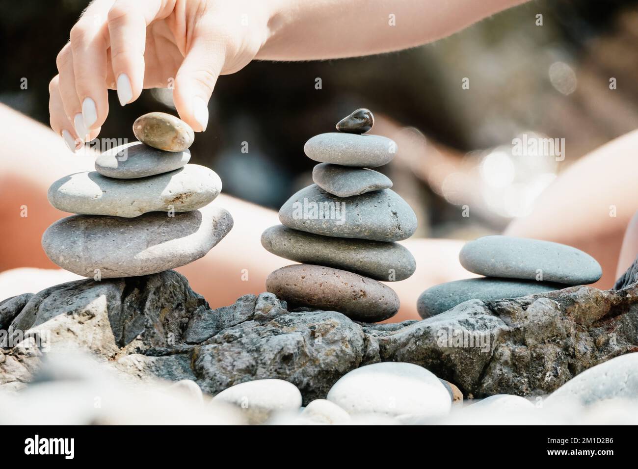 Woman with daughter bilds stones pyramid on seashore on a sunny day on ...