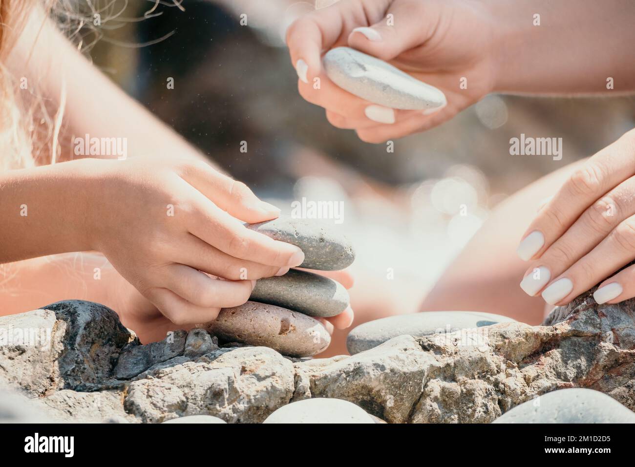 Woman with daughter bilds stones pyramid on seashore on a sunny day on ...