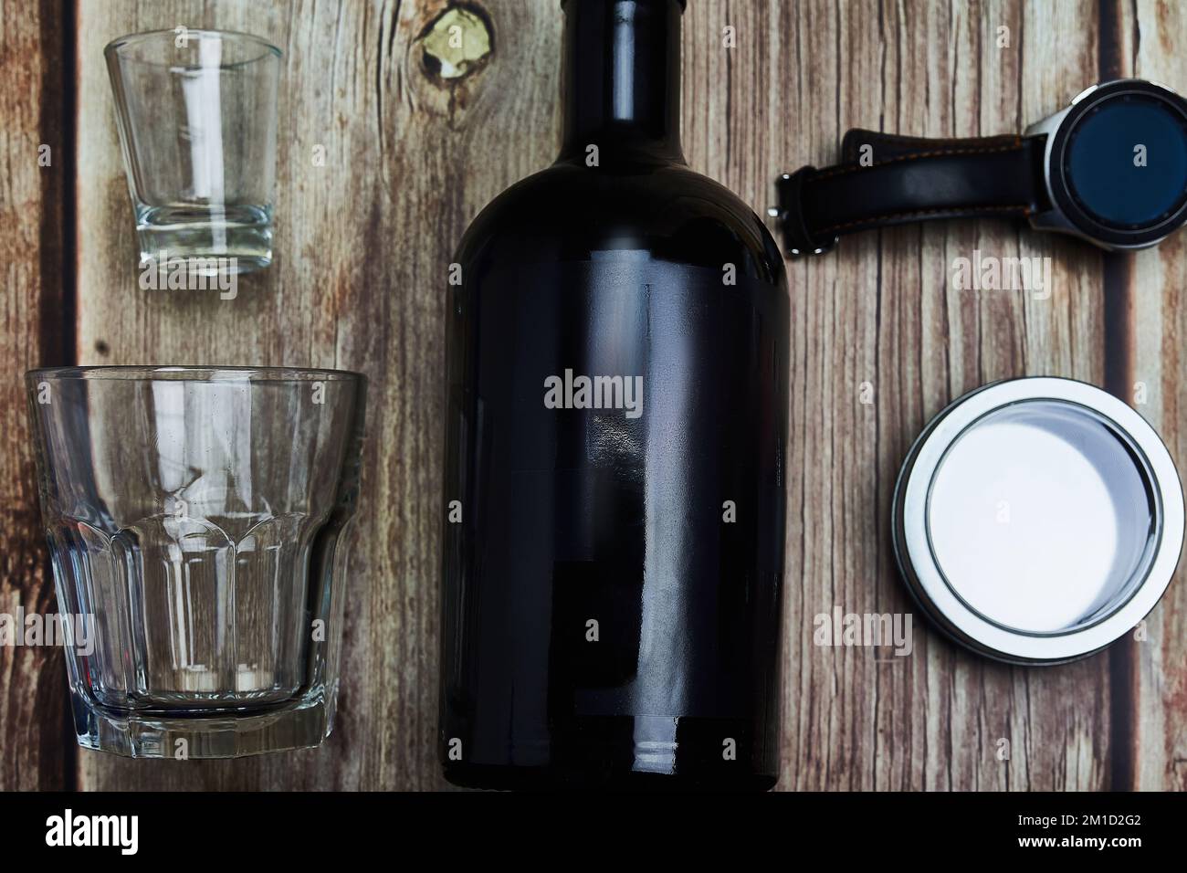 shot glass tin can worn smart watch and a bottle of alcohol on wood ...