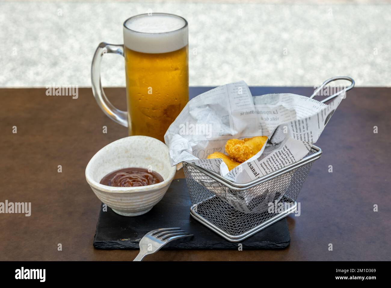 A closeup of fried chicken nuggets served with ketchup and beer in a ...