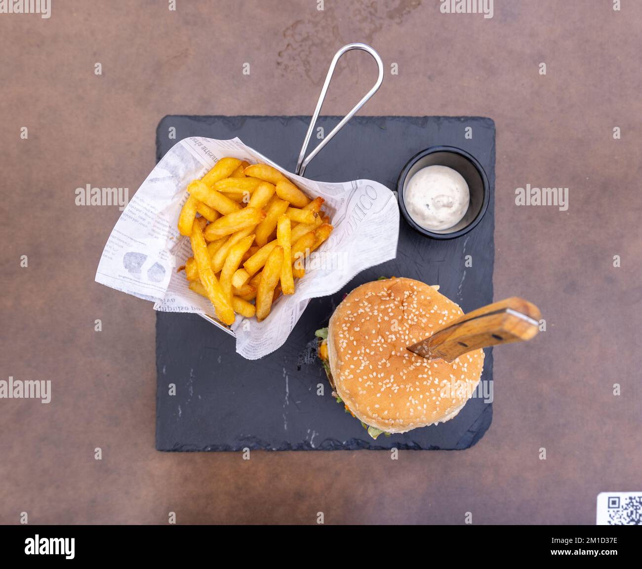 A top view of a burger served with French fries and a sauce in a ...