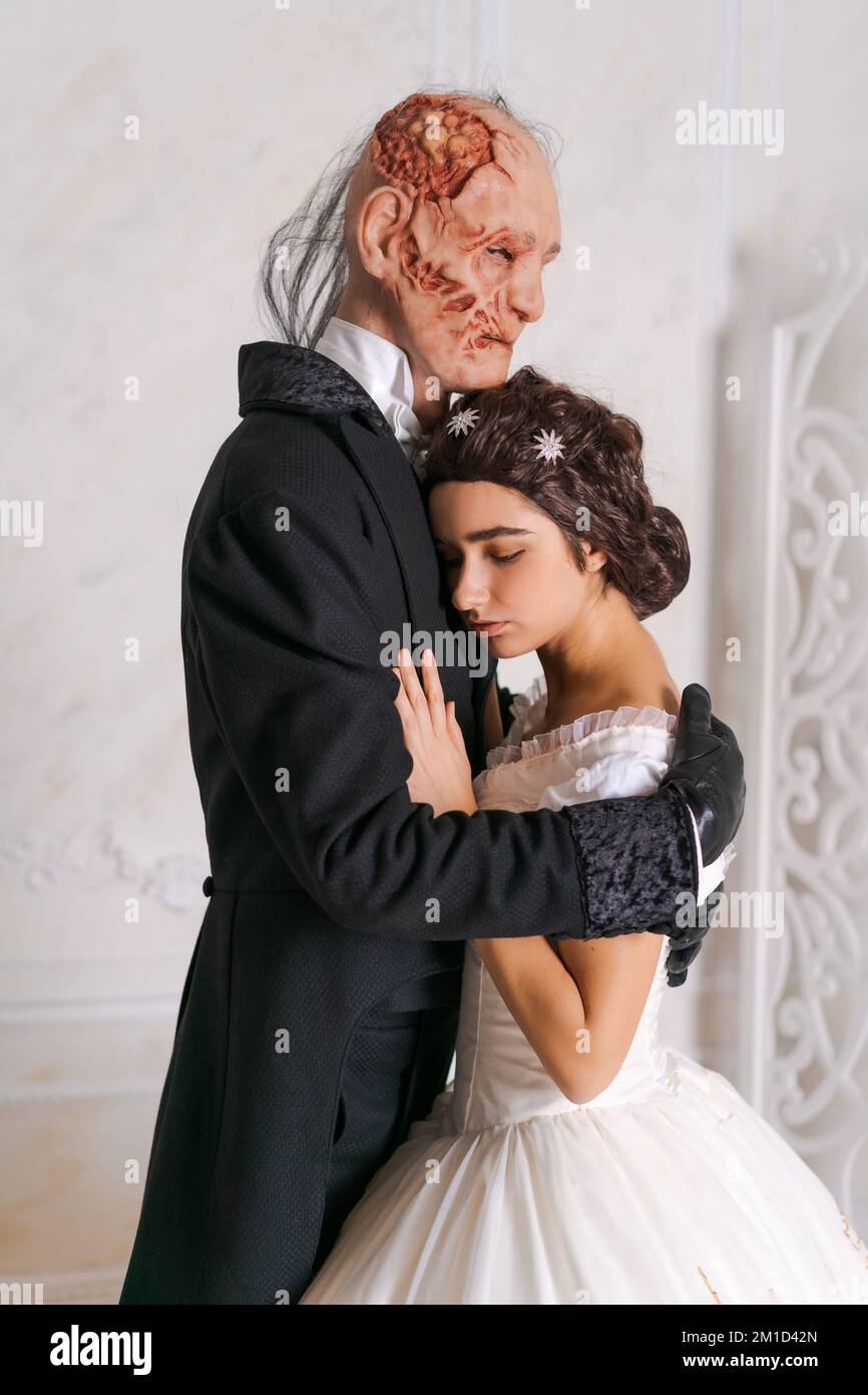 Beautiful girl in white dress and scary disfigured man in black stand ...