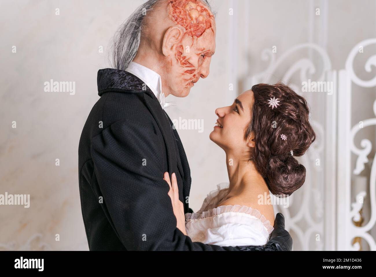 Beautiful girl in white dress and scary disfigured man in black stand ...