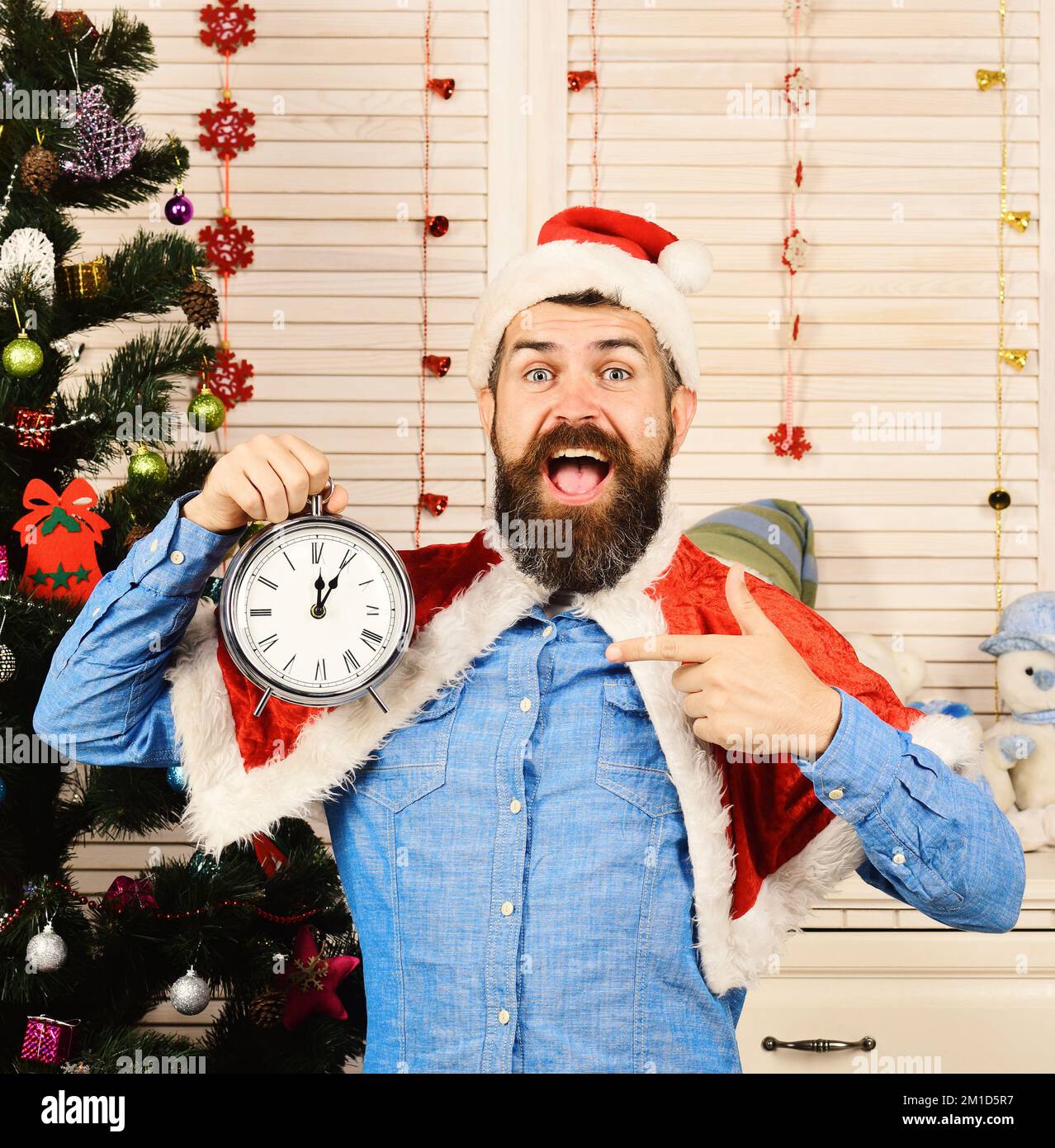 Guy in hat and red cape points at alarm clock Stock Photo - Alamy