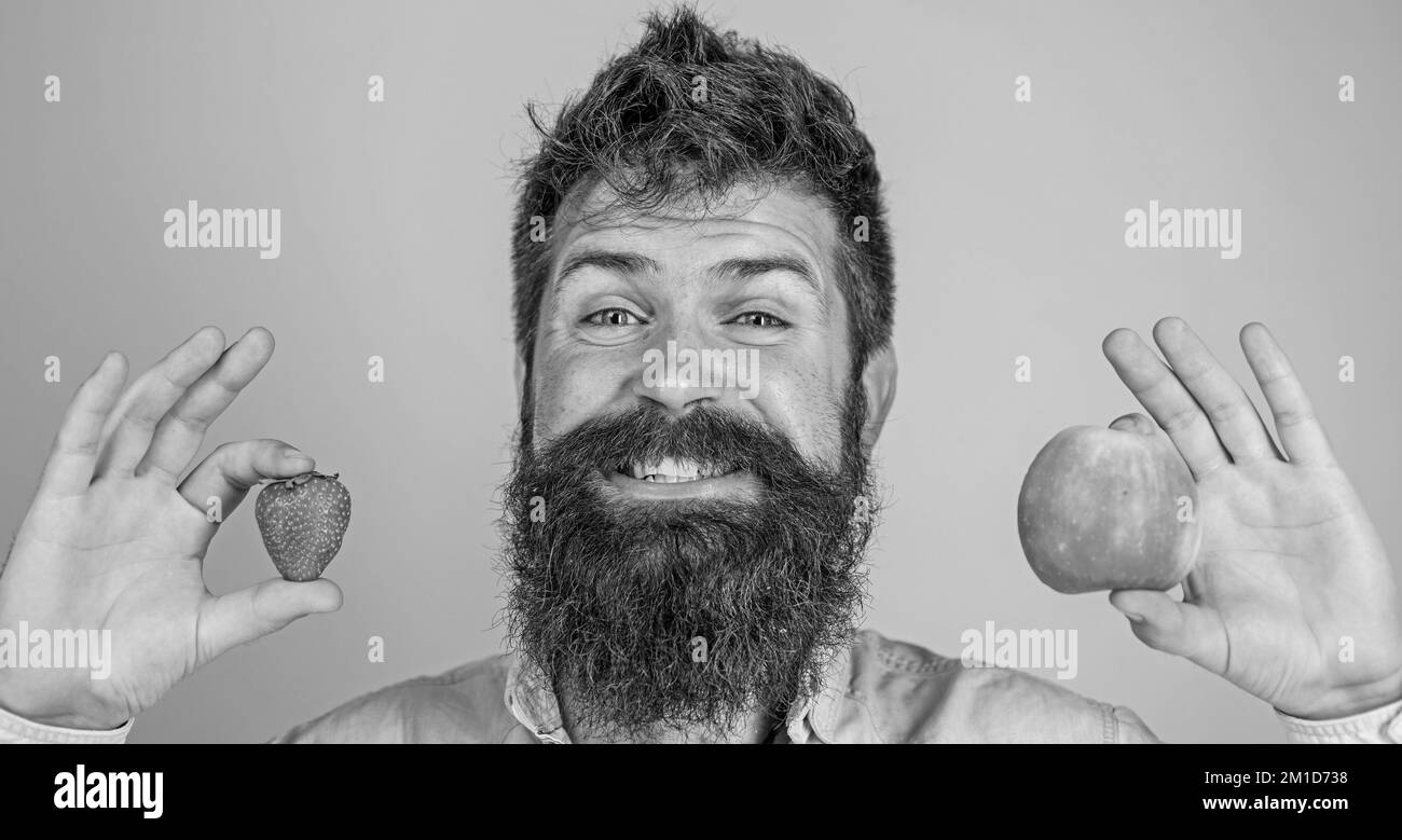 Summertime benefits. Man bearded smiling holds apple and strawberry in ...