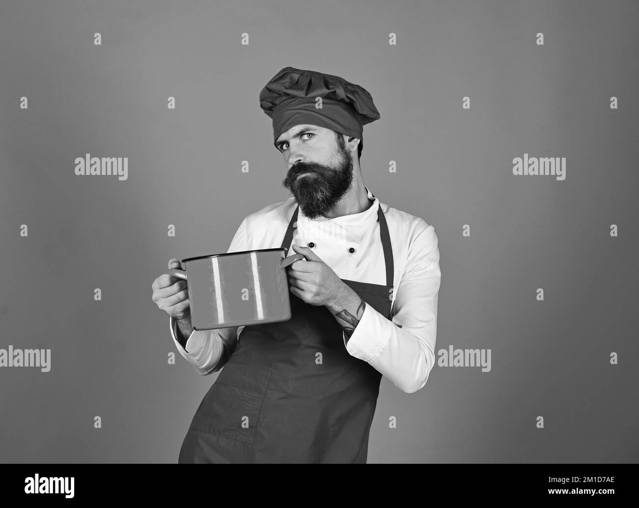 Cook with surprised face in burgundy uniform holds soup pot Stock Photo ...