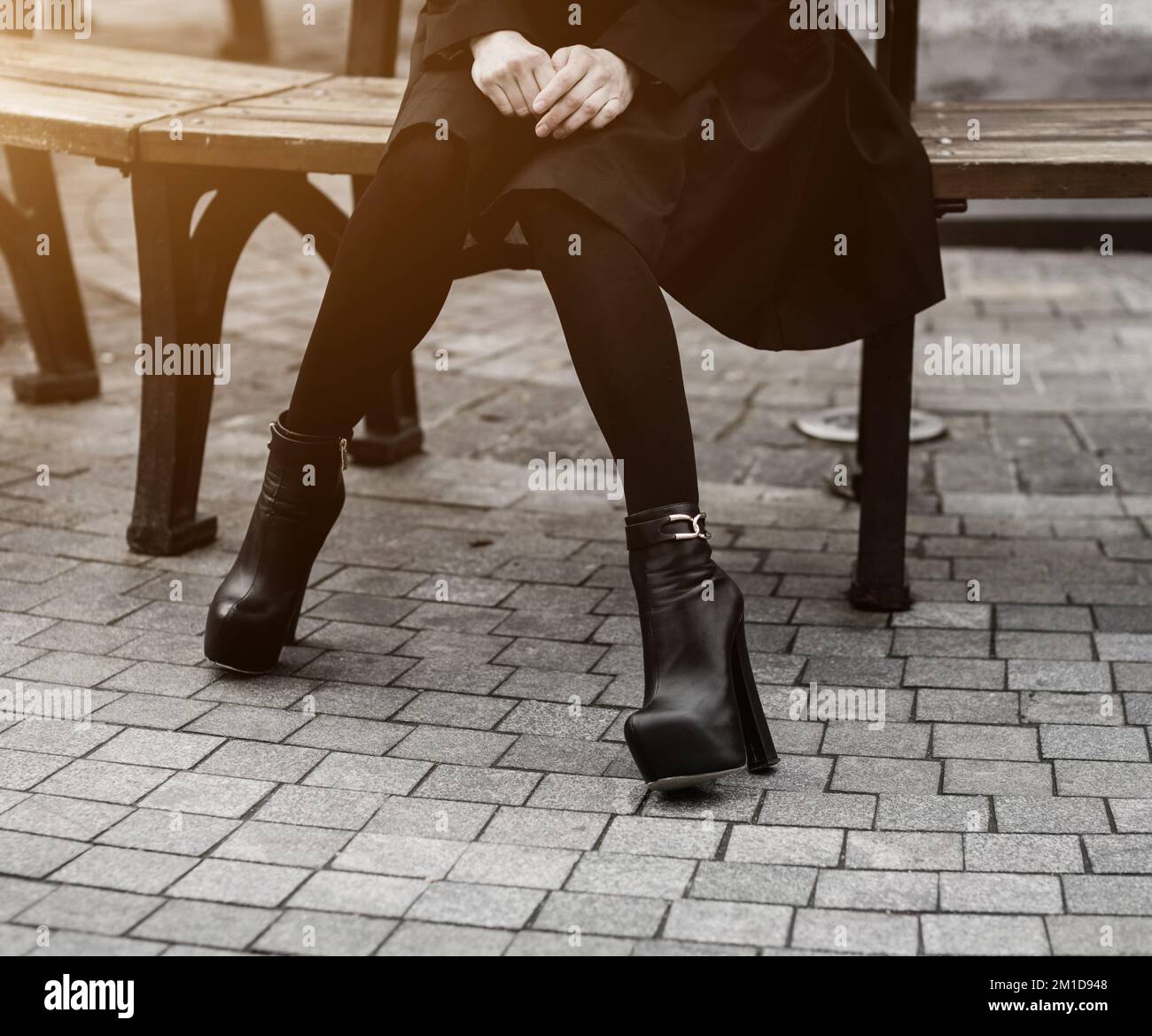 woman in black coat and leather boots with heel sitting on bench Stock ...