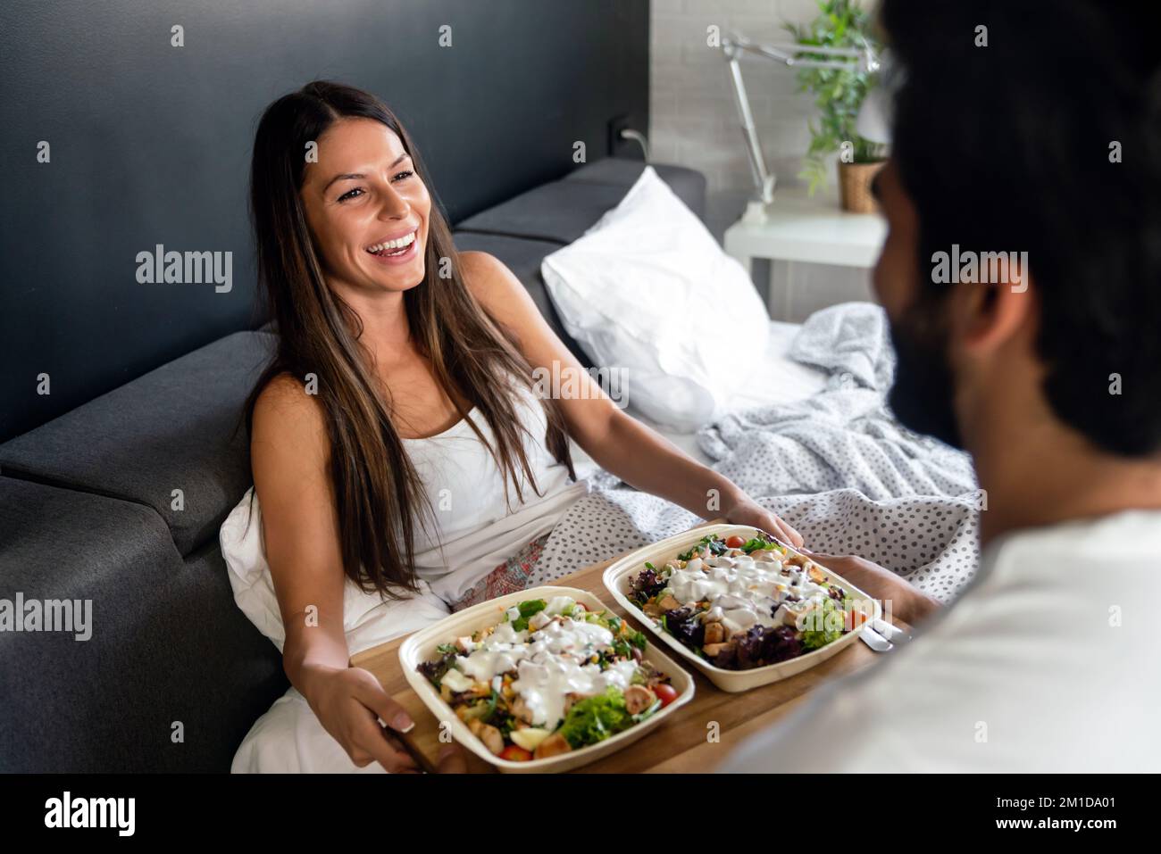 Young romantic man brings breakfast to woman in the bed and laughing ...