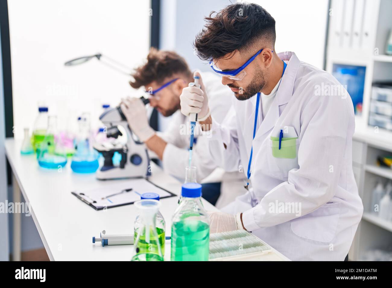Young couple wearing scientist uniform using microscope and pipette at ...