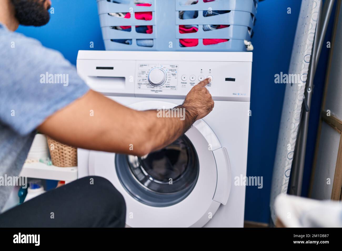 Young hispanic man turning on washing machine at laundry room Stock ...
