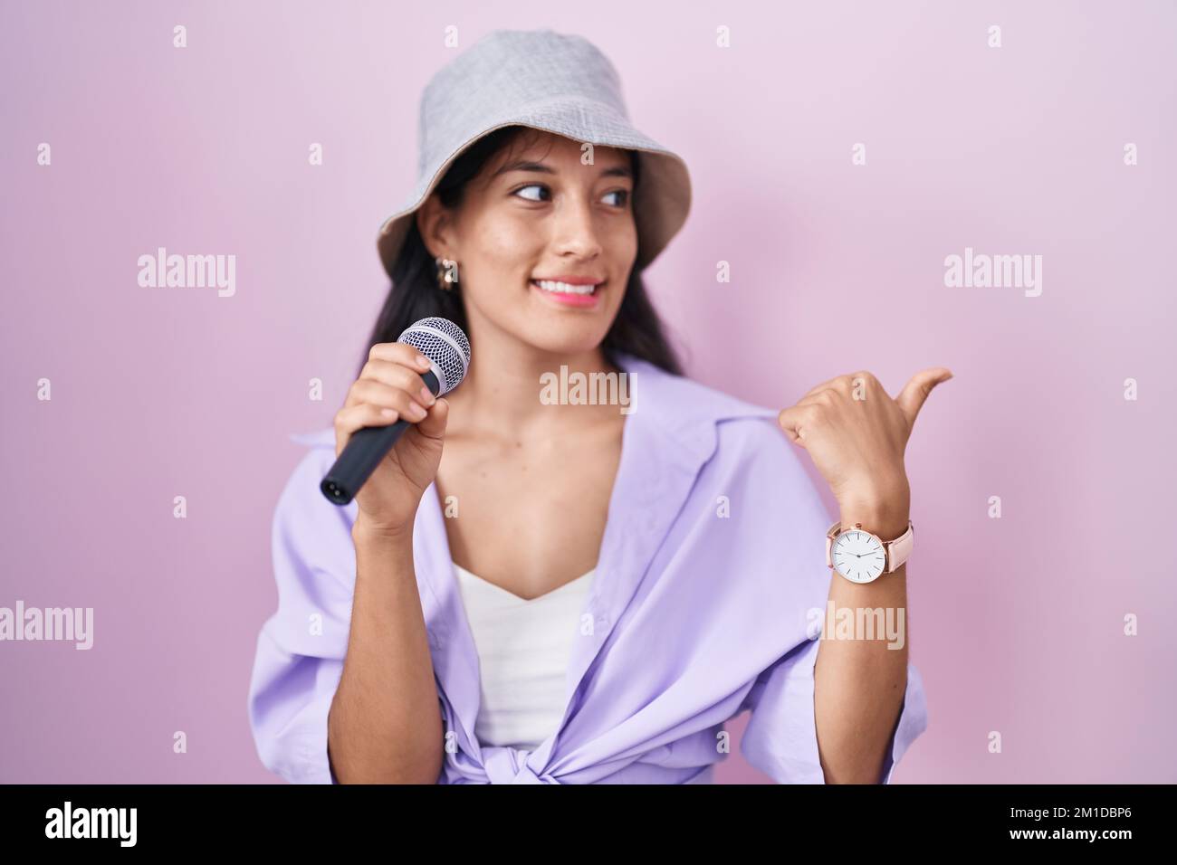 Young hispanic woman singing song using microphone over pink background ...