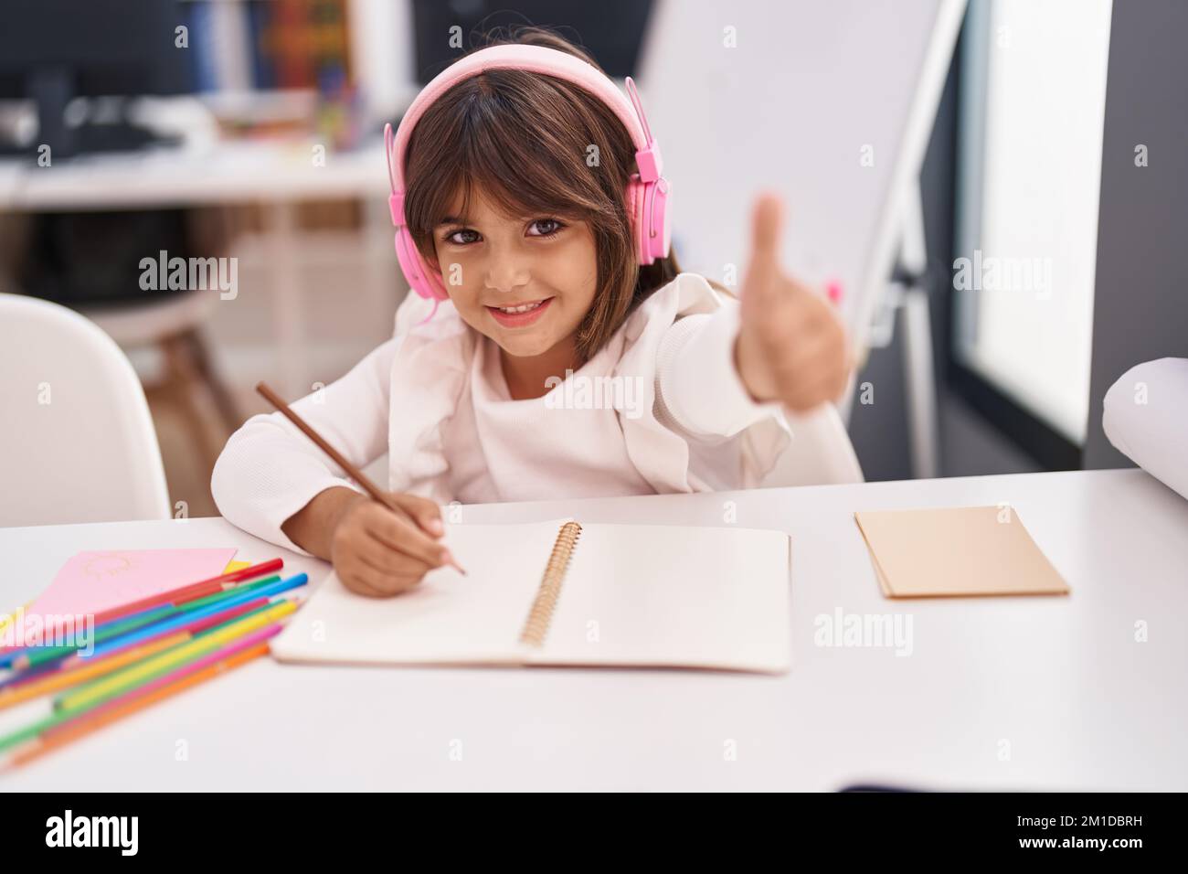 Adorable hispanic girl student listening to music writing on notebook ...
