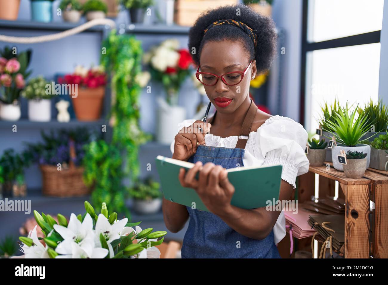 African american woman florist reading notebook with doubt expression ...