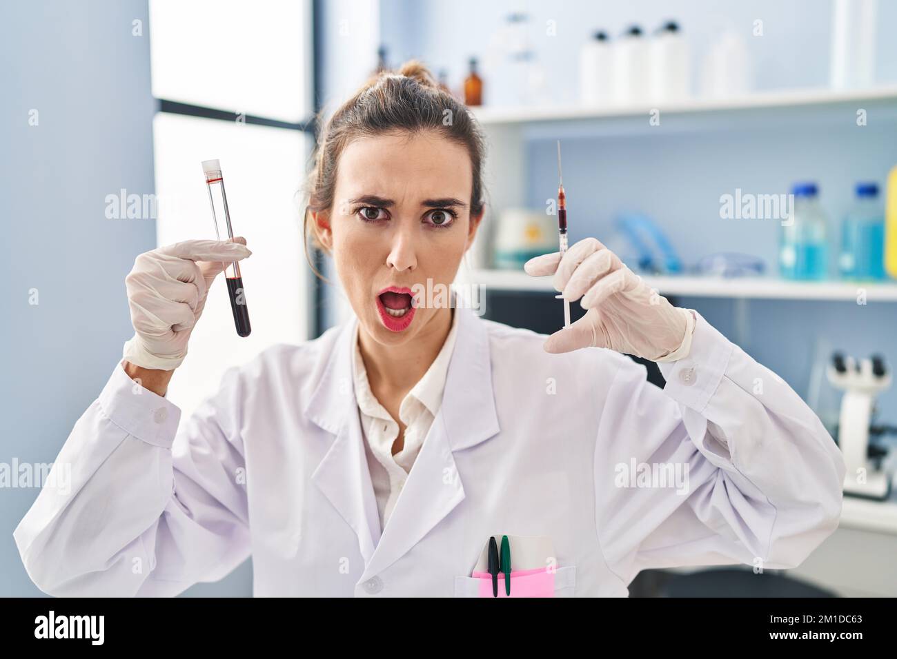 Young woman working at scientist laboratory holding blood sample in ...