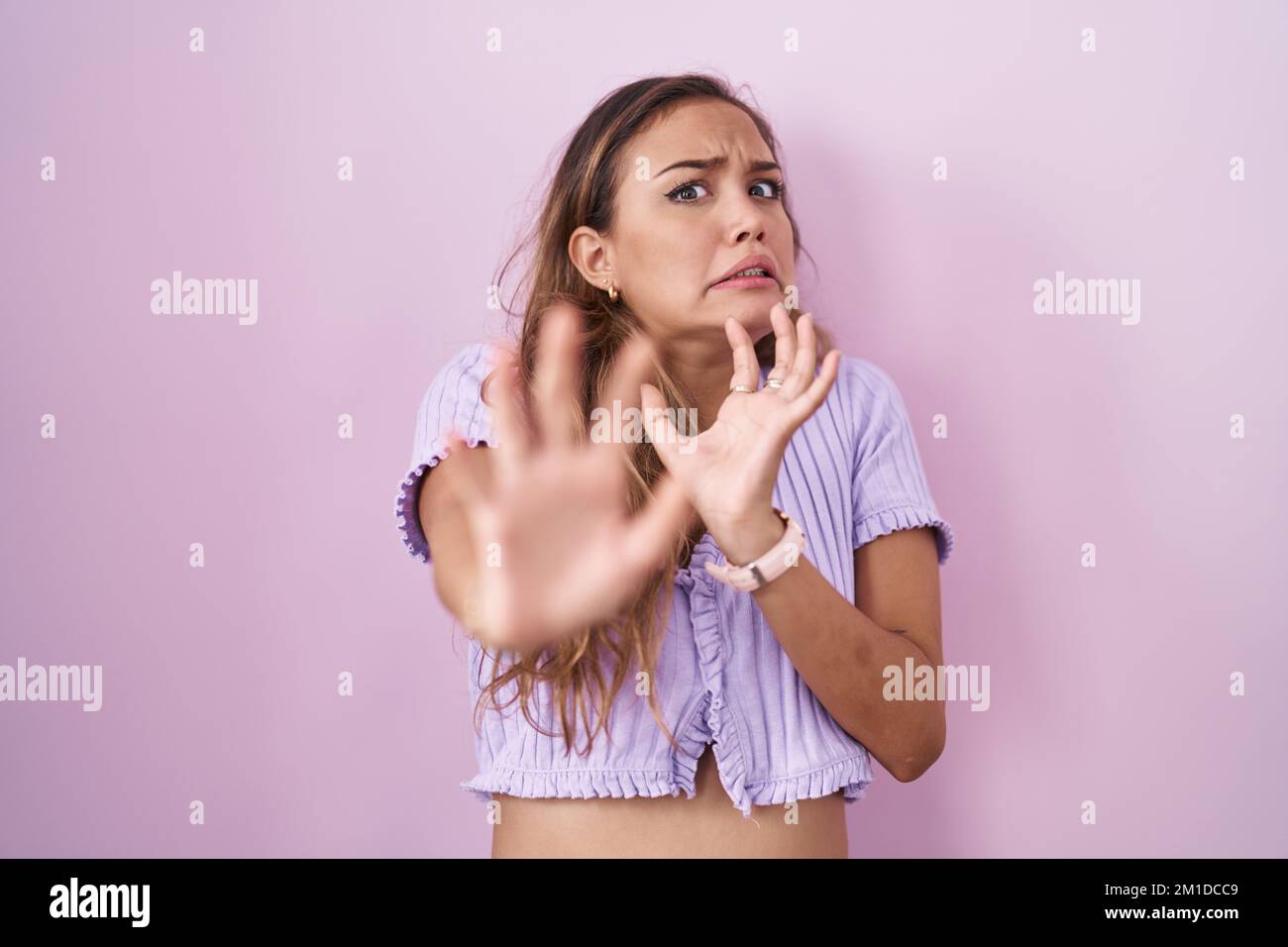 Young hispanic woman standing over pink background afraid and terrified ...