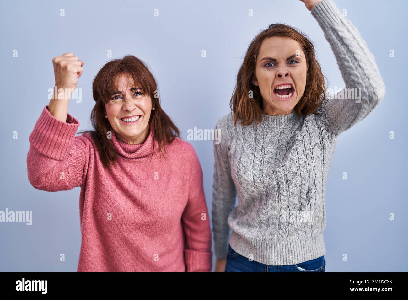 Mother and daughter standing over blue background angry and mad raising ...