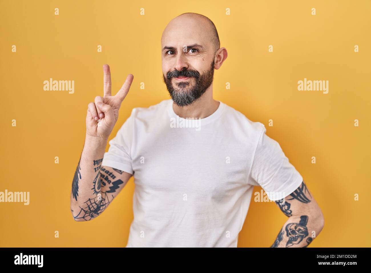 Young hispanic man with tattoos standing over yellow background smiling ...