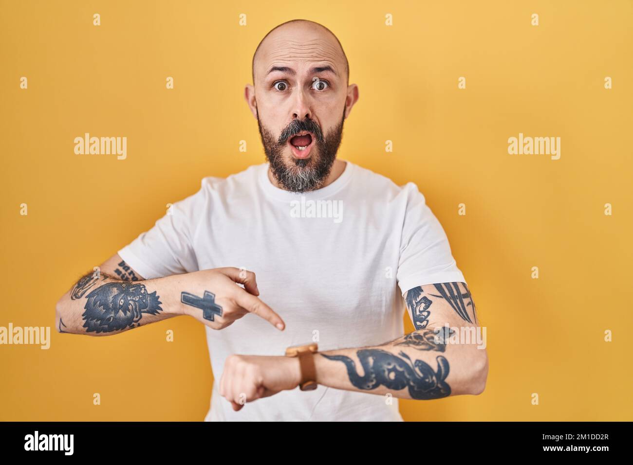 Young hispanic man with tattoos standing over yellow background in ...