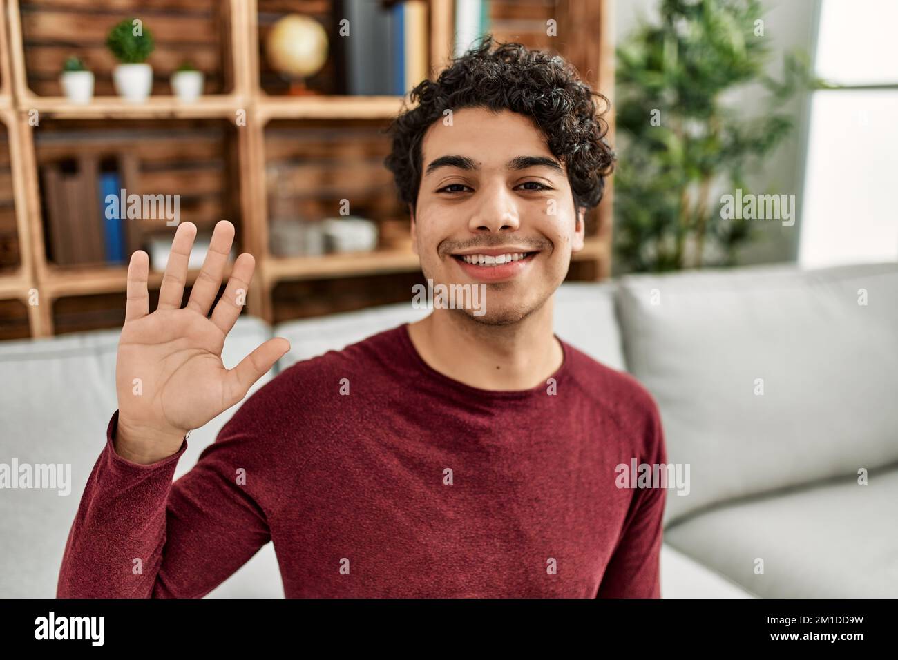 Young hispanic man smiling happy saying hello with hand at home Stock ...