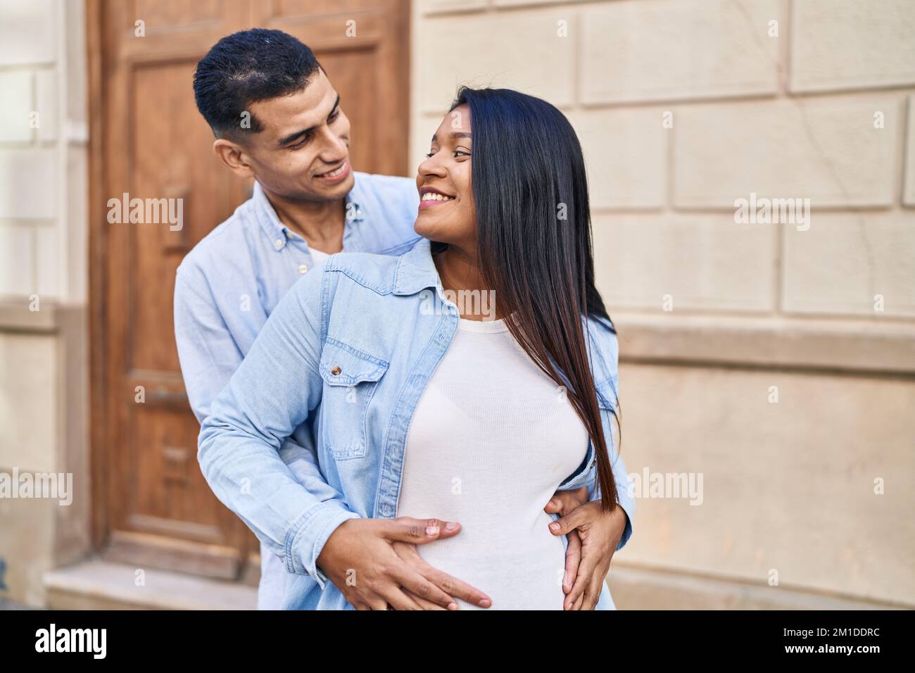 Young latin couple expecting baby hugging each other standing at street Stock Photo - Alamy