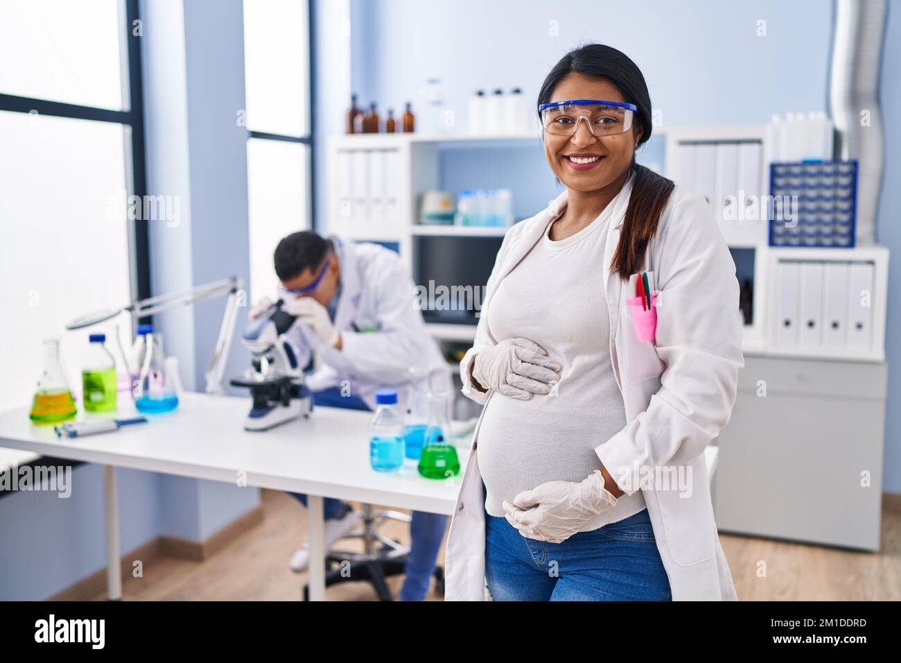 Young hispanic woman expecting a baby working at scientist laboratory ...