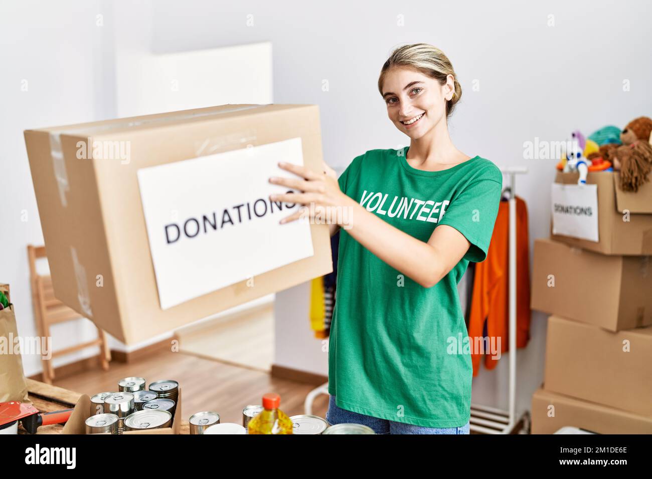 Young caucasian woman wearing volunteer uniform holding donations box ...