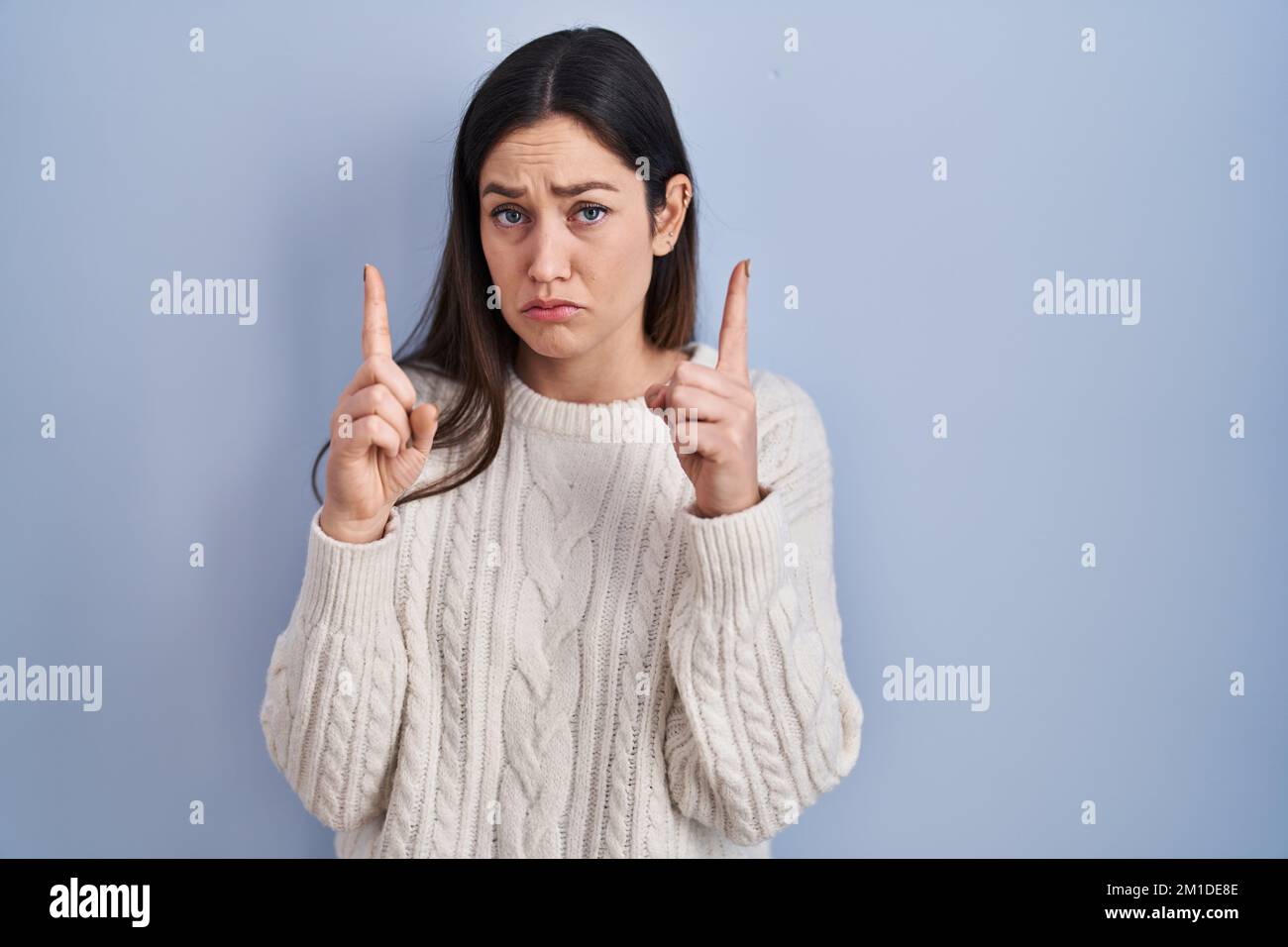 Young brunette woman standing over blue background pointing up looking ...