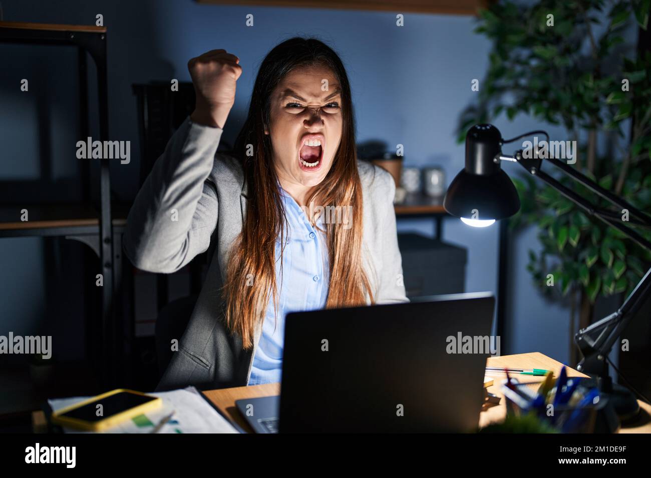 Young brunette woman working at the office at night angry and mad ...
