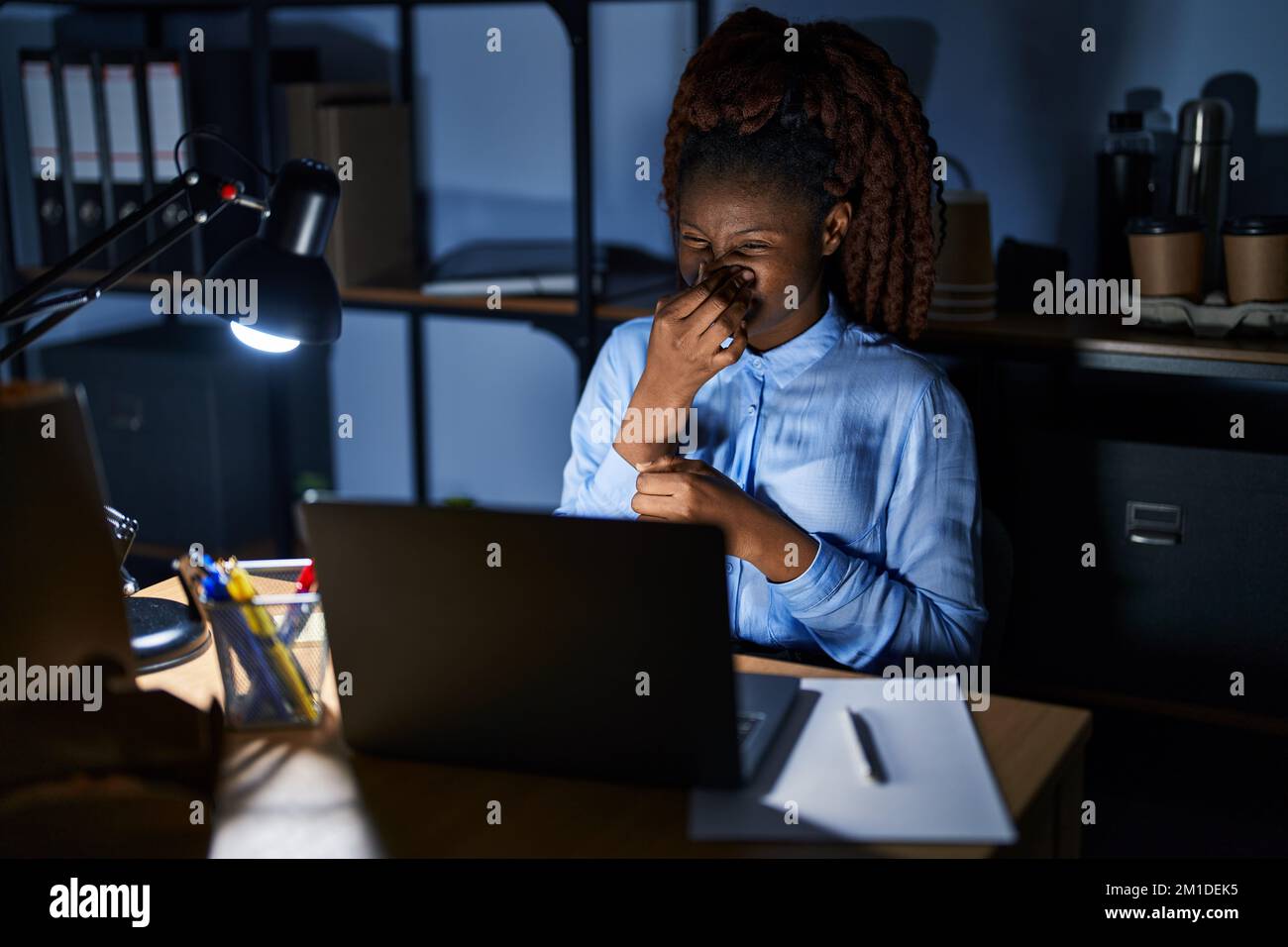 African woman working at the office at night smelling something stinky ...