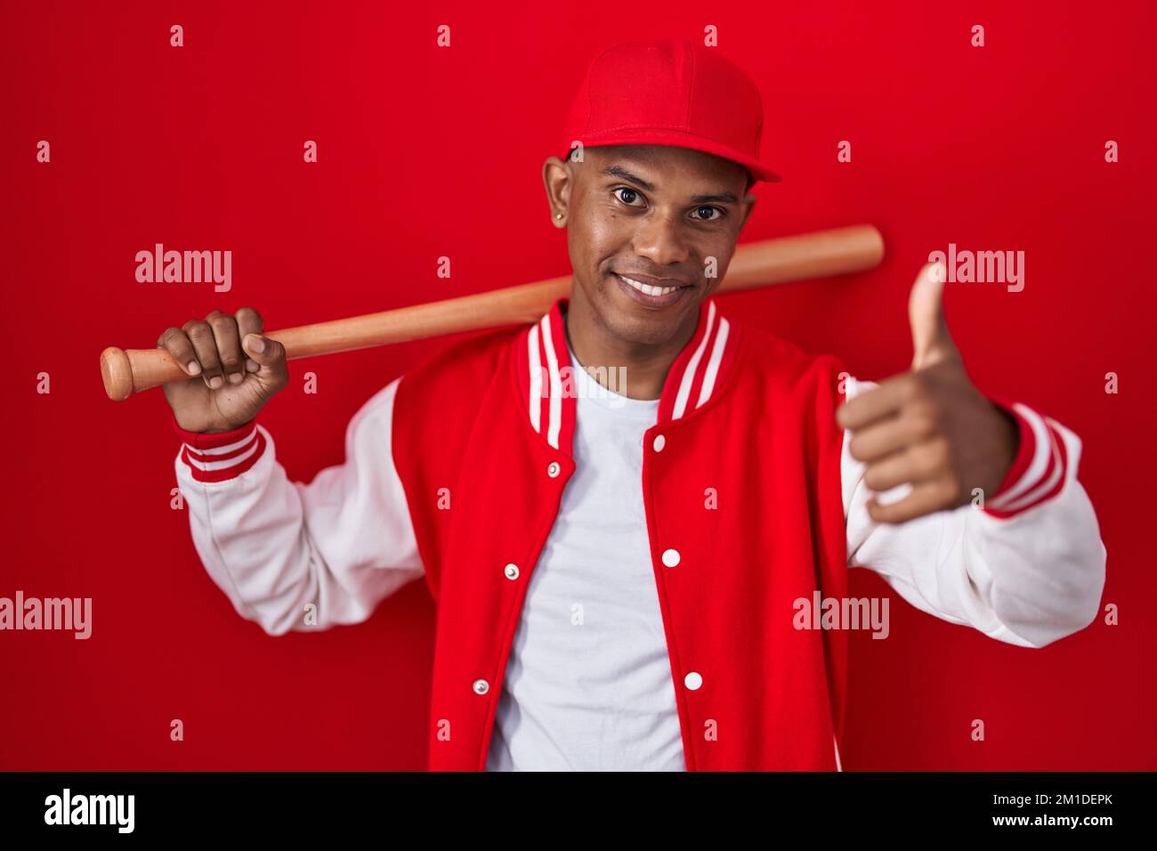Young hispanic man playing baseball holding bat approving doing ...
