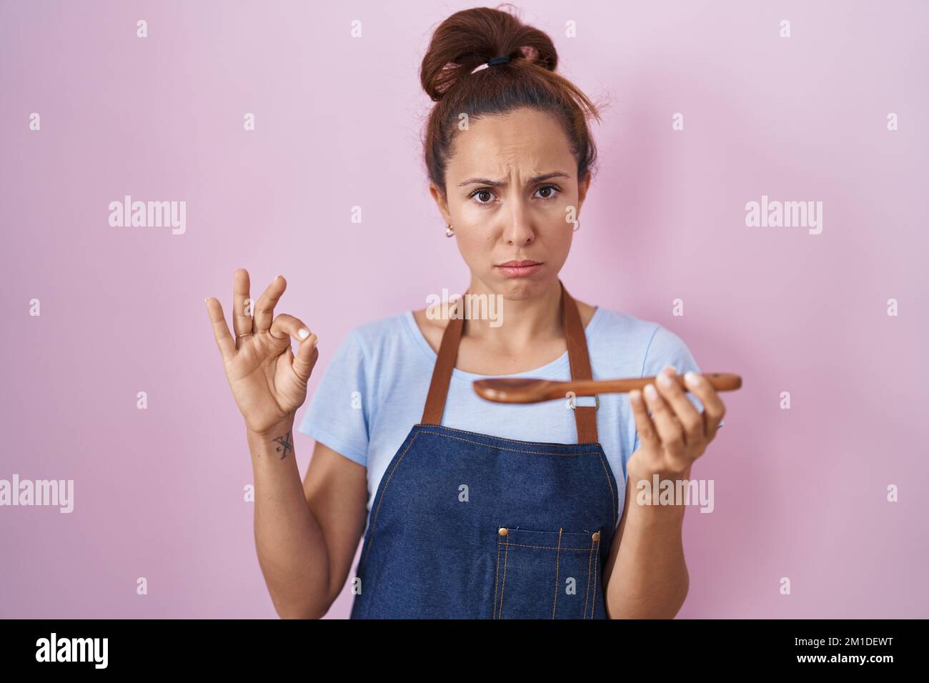Brunette woman wearing professional cook apron holding wooden spoon ...
