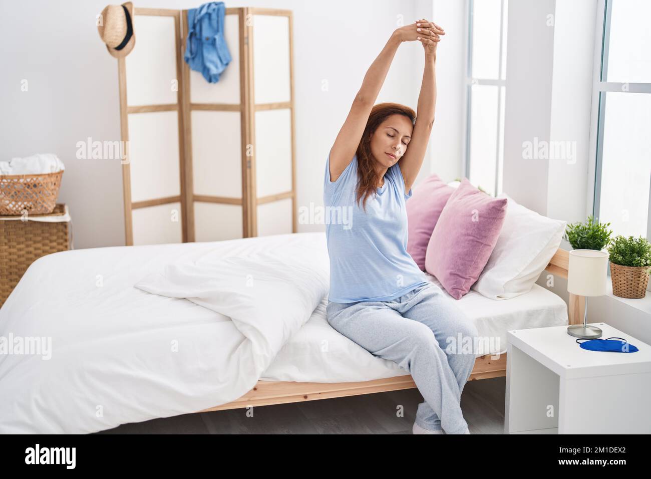 Young woman stretching arms sitting on bed at bedroom Stock Photo - Alamy