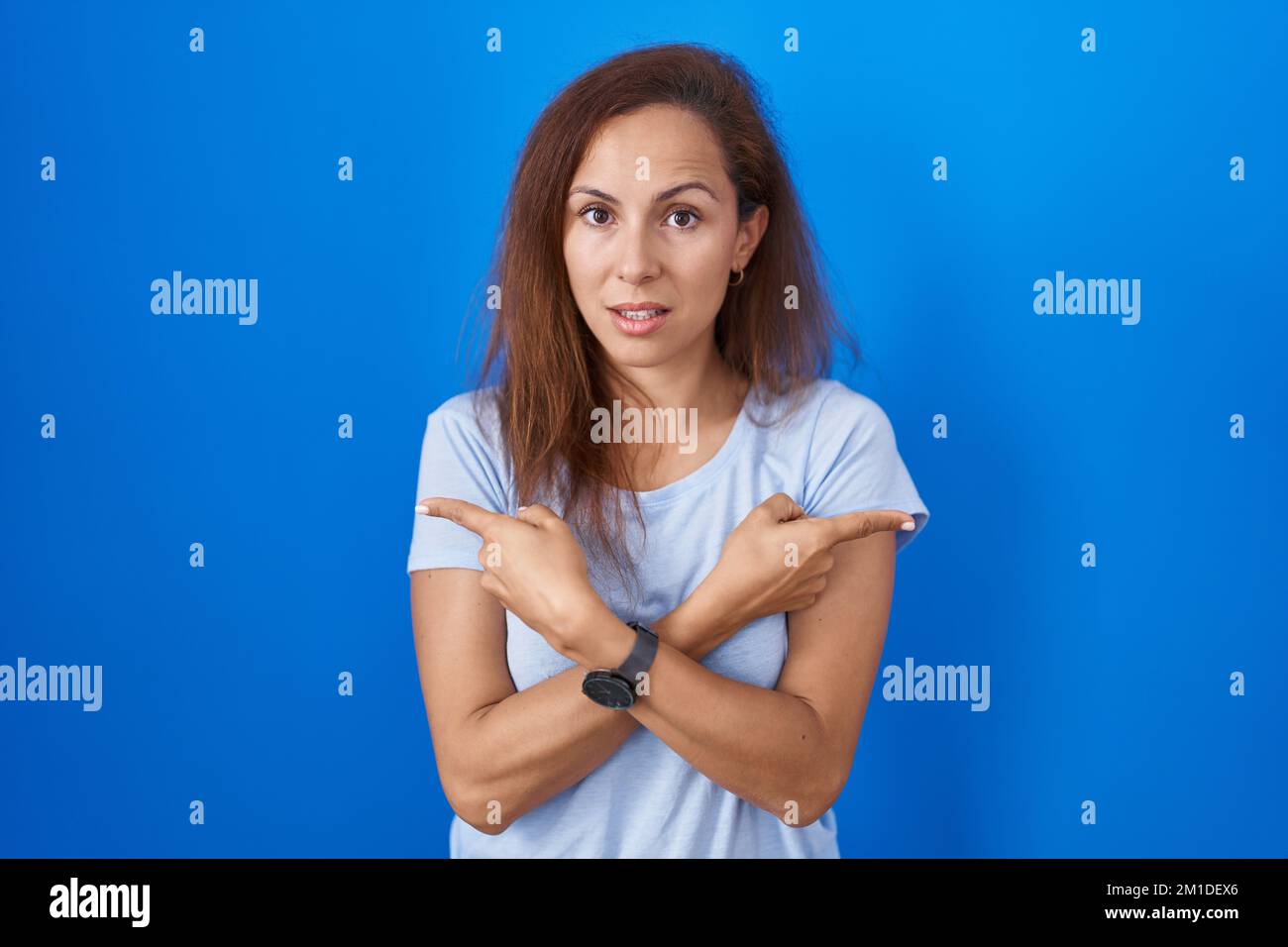 Brunette woman standing over blue background pointing to both sides ...