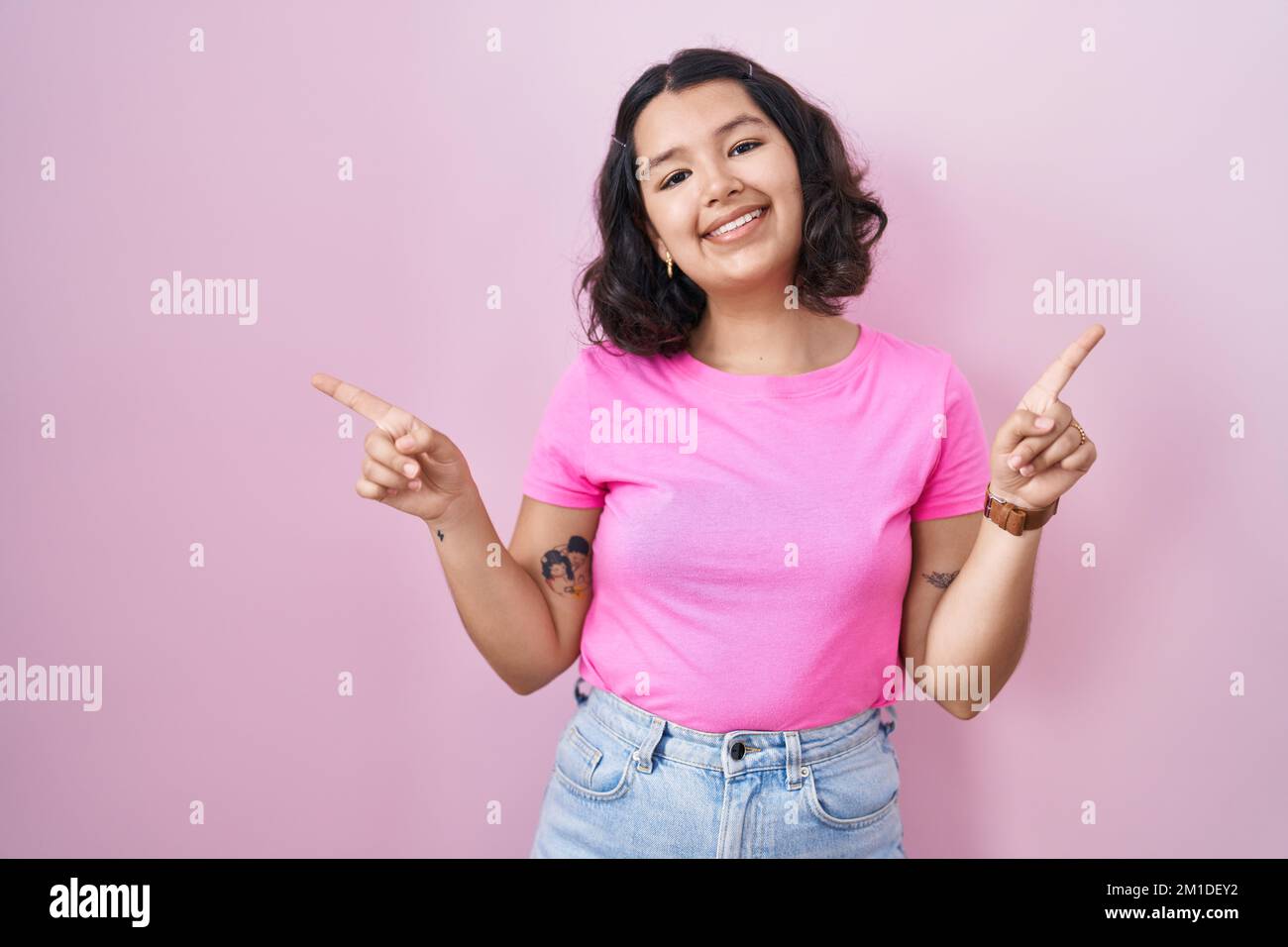 Young hispanic woman standing over pink background smiling confident ...