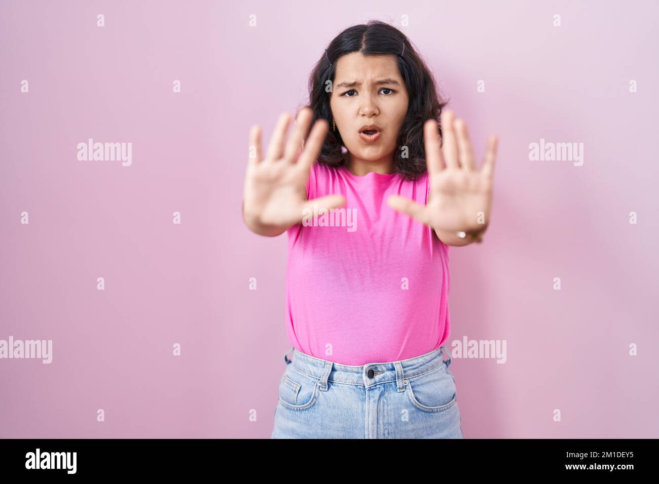 Young hispanic woman standing over pink background doing stop gesture ...