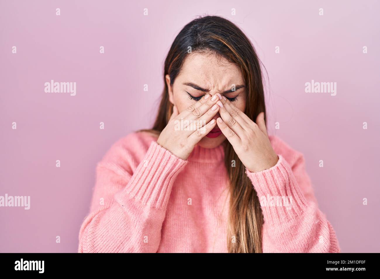 Young hispanic woman standing over pink background rubbing eyes for ...